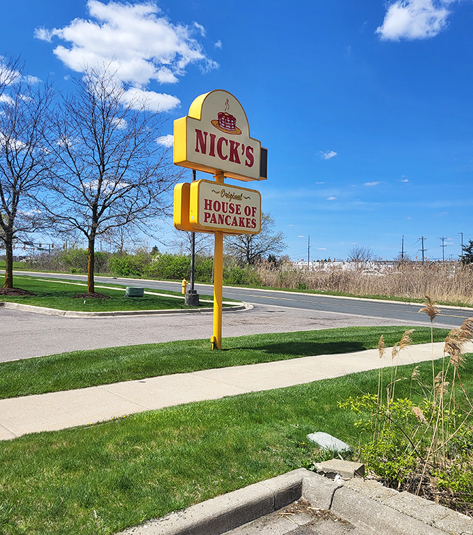 The roadside sign stands tall against Michigan skies, a yellow and red promise that pancake perfection awaits just a turn of the steering wheel away.