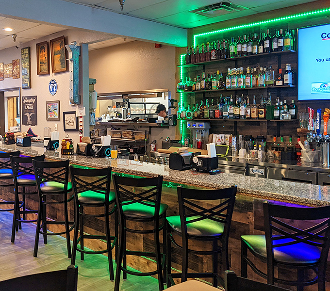 The bar area glows with promise, offering liquid companions for your BBQ feast. Green lighting makes everything feel like a special occasion. 