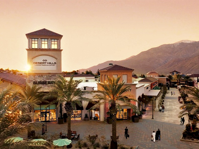 As the desert sun sets behind the mountains, Desert Hills transforms from daytime shopping marathon to evening retail therapy session under palm tree silhouettes.