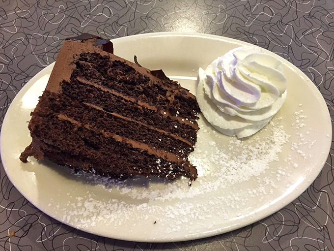 Chocolate cake layered so tall it requires engineering degrees to cut, topped with whipped cream clouds.