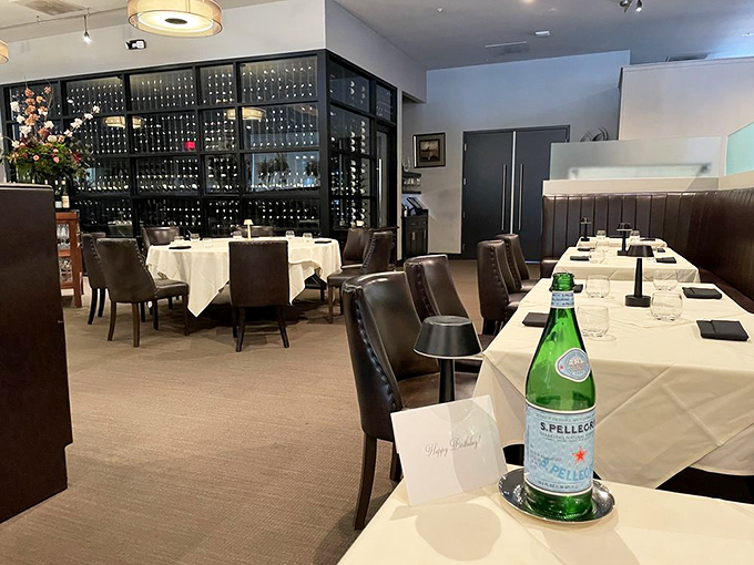 Pristine dining room with wine storage walls - where white tablecloths meet dark leather in perfect steakhouse harmony.