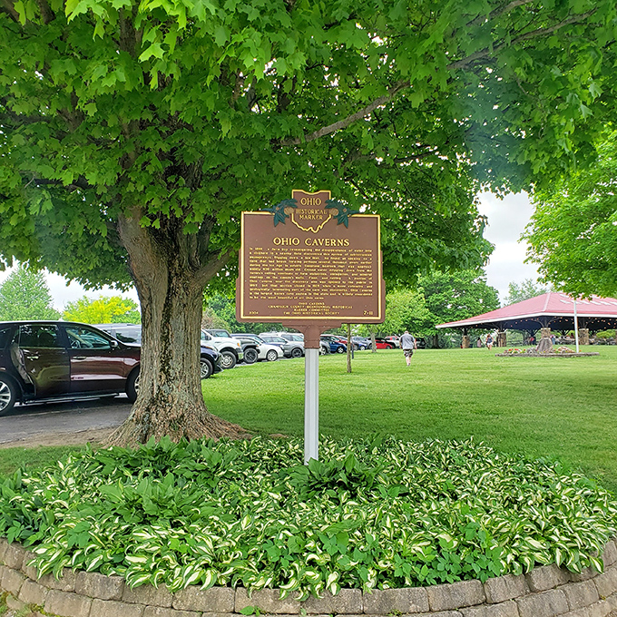 This historical marker stands sentinel under leafy shade, a humble signpost to the underground wonderland that has amazed visitors for generations.