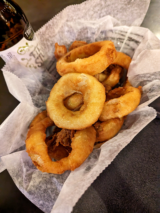 Golden onion rings provide satisfying crunch without greasiness, exemplifying how classic bar food can be executed with professional excellence.