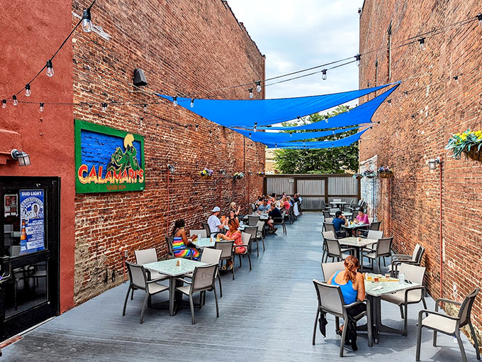 The outdoor patio creates an urban oasis between brick walls, where blue canopies and string lights transform alfresco dining into a magical experience.