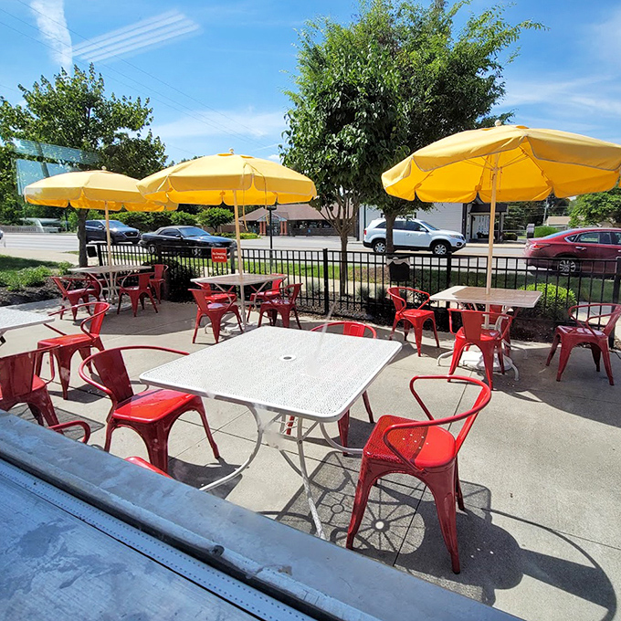 Cheerful yellow umbrellas and cherry-red chairs create an outdoor dining space that feels like summer incarnate, even on a cloudy day.