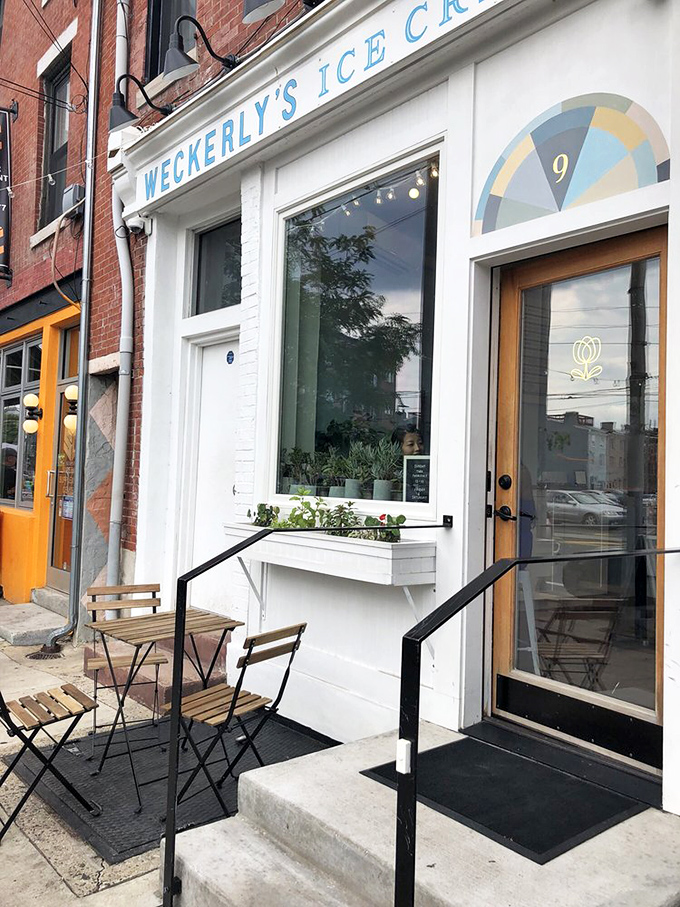 A small ice cream shop with a cozy outdoor seating area features a few wooden tables and chairs set along the sidewalk.