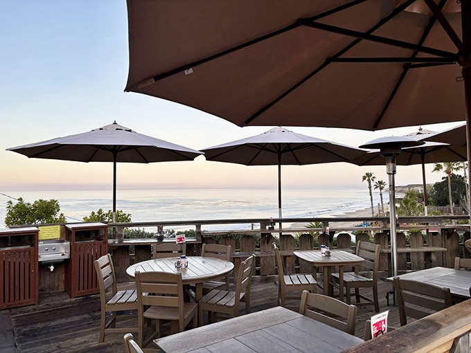 The million-dollar view that makes every bite taste better—wooden tables under umbrellas where the Pacific Ocean serves as both backdrop and dining companion.