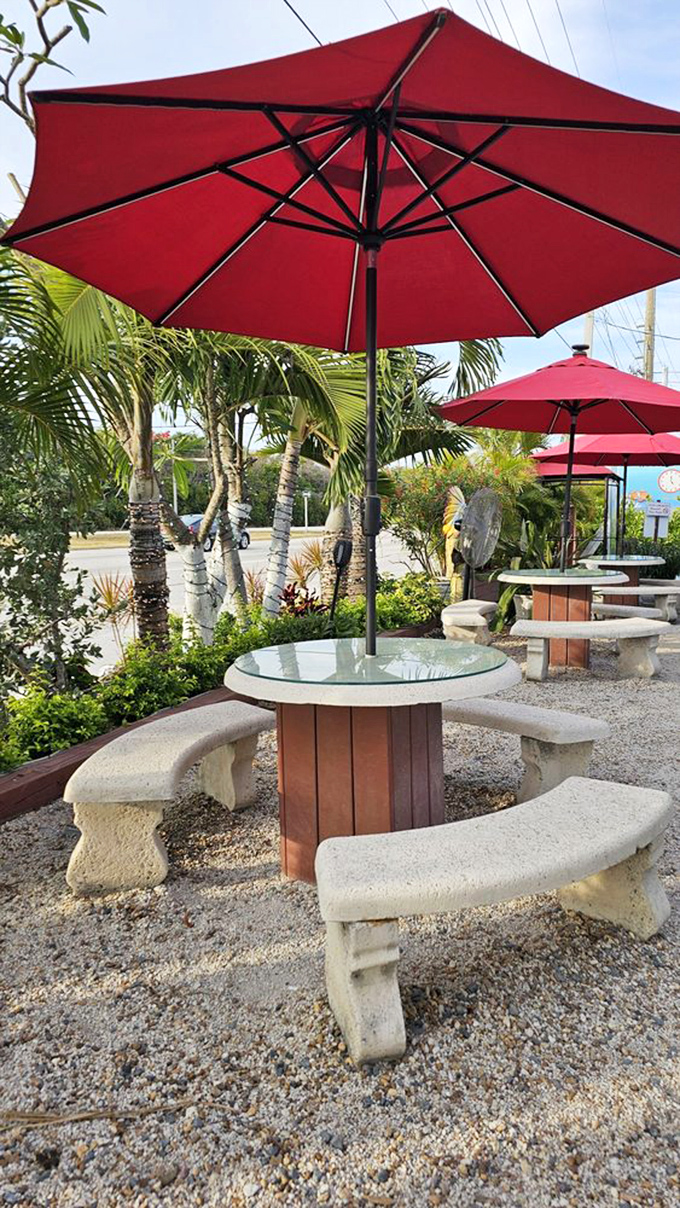 Outdoor seating under crimson umbrellas offers a tropical oasis where palm trees sway and seafood feasts await on circular stone tables.