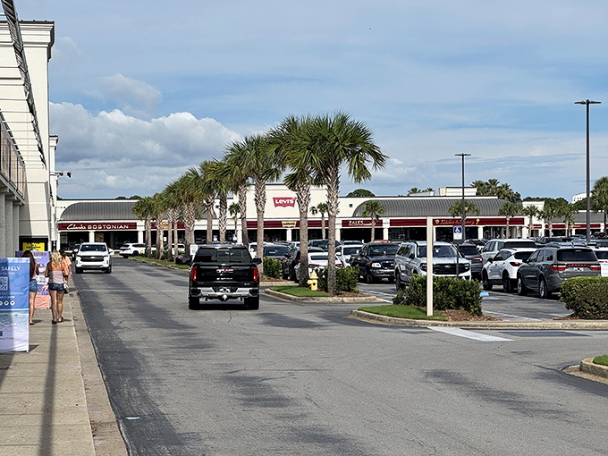 Palm trees stand sentinel over rows of parked cars, each filled with shopping bags and the satisfied exhaustion that only a successful outlet expedition brings.