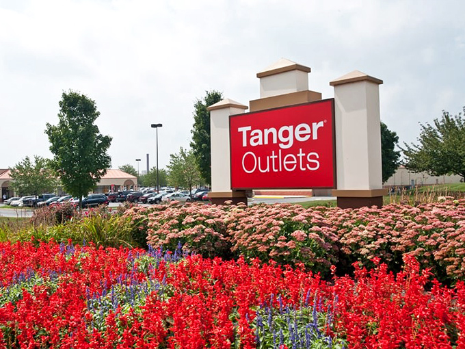 Tanger's entrance sign blooms with promise and petunias. The landscaping is as carefully curated as the stores within.