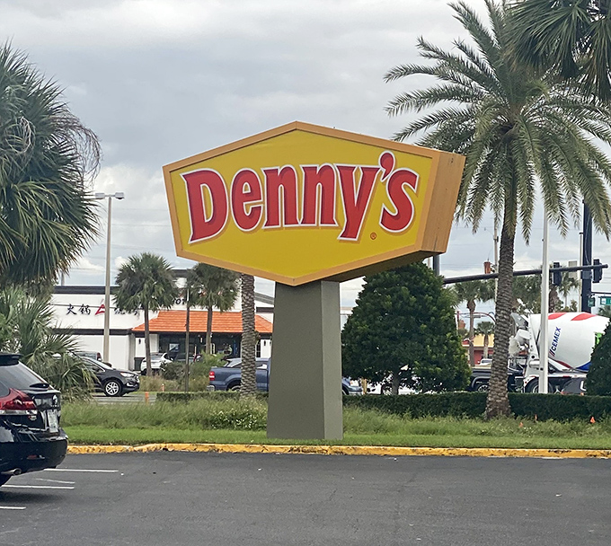 The sign stands tall among palm trees, a yellow-and-red beacon announcing "Yes, we're open" to travelers from every time zone simultaneously.
