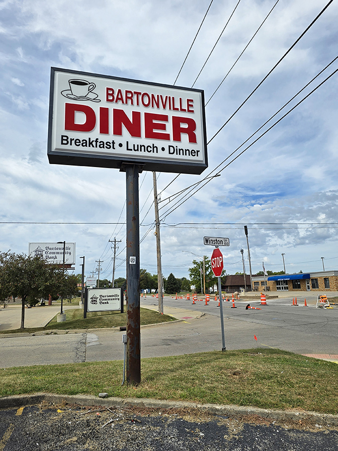 The roadside sign proudly announces "Breakfast &bull; Lunch &bull; Dinner" &ndash; the holy trinity of diner offerings. That coffee cup icon is practically winking at early risers driving by.