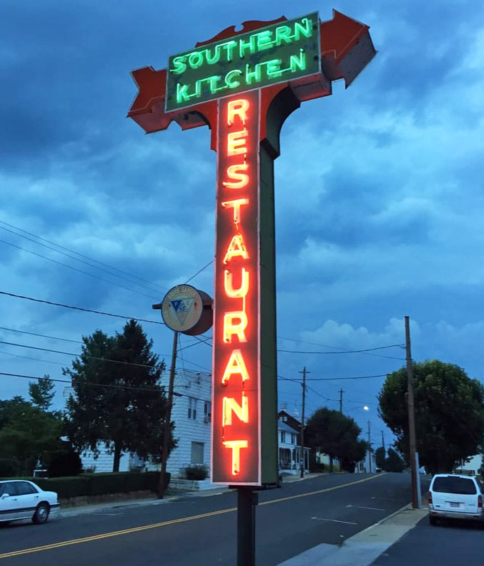 As evening falls, the neon sign glows like a lighthouse for hungry travelers &ndash; "SOUTHERN KITCHEN RESTAURANT" in electric red and green against the twilight sky.