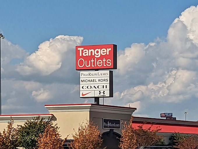 The towering Tanger sign against dramatic clouds, listing luxury brands that await inside. Like a modern-day retail Stonehenge, but with better parking.