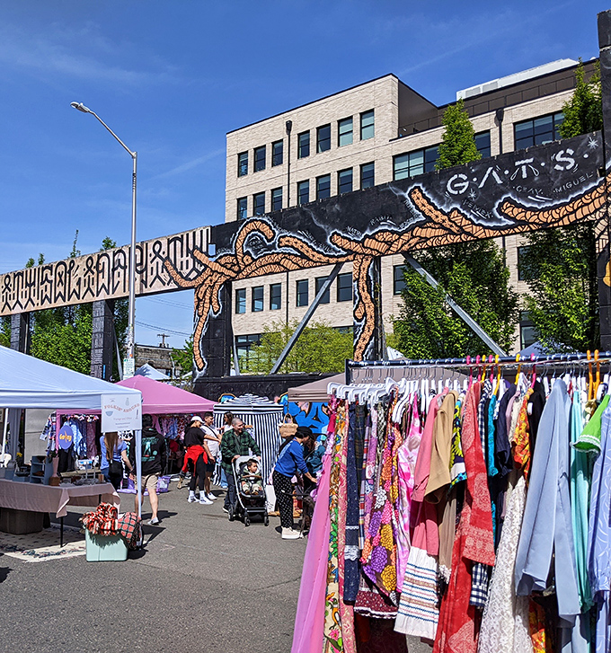 Vibrant clothing racks under a mural-adorned backdrop &ndash; Portland's artistic spirit shines at this hip outdoor market.