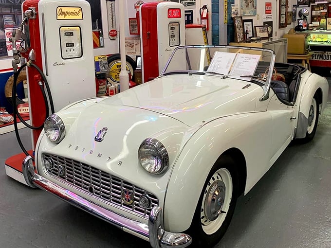 This elegant white Triumph TR3 poses between vintage gas pumps, like a British aristocrat who accidentally wandered into an American sock hop.