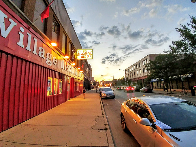 As evening falls, the iconic Village Discount sign glows like a beacon for night owls seeking last-minute treasure hunts.