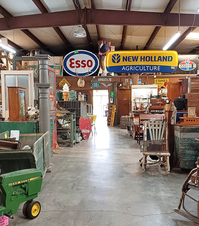 Vintage signs hang like colorful clouds overhead, guiding treasure hunters through aisles where Esso and New Holland logos reign supreme over carefully curated chaos.