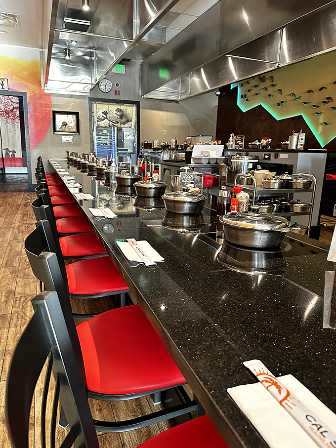 The sleek counter setup is dinner theater in the round—each diner gets their own hot pot stage for culinary performance art.