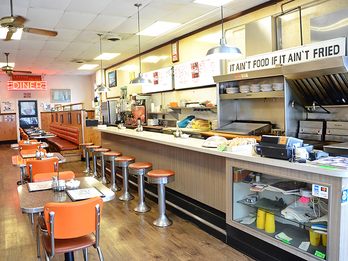 Classic diner perfection: chrome stools, orange seats, and that sign declaring "IT AIN'T FOOD IF IT AIN'T FRIED" &ndash; the Eleventh Commandment of comfort cuisine.