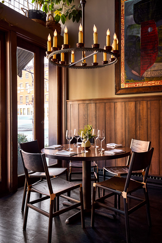 Warm wooden paneling meets medieval-inspired lighting in this intimate corner. The circular chandelier casts a glow that makes everyone look like they're starring in their own food documentary.