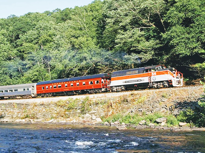 Where river meets rail: The vibrant orange passenger car hugs the shoreline, offering riders front-row seats to Pennsylvania's pristine waterways. Smartphones simply can't capture this magic.