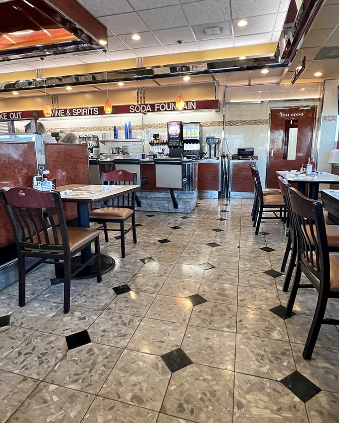 Classic diner aesthetics meet comfortable functionality inside, where diamond-patterned floors and warm lighting create the perfect backdrop for memorable meals.