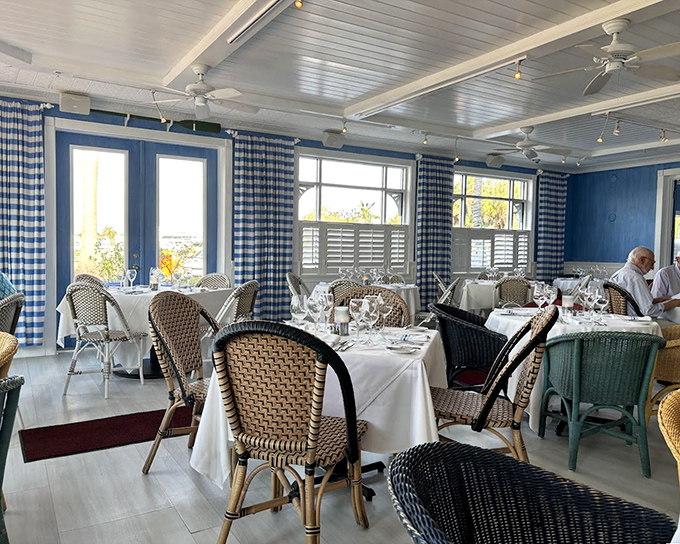 Crisp white tablecloths meet casual wicker chairs in a dining room that feels like the French Riviera took a vacation to Florida.