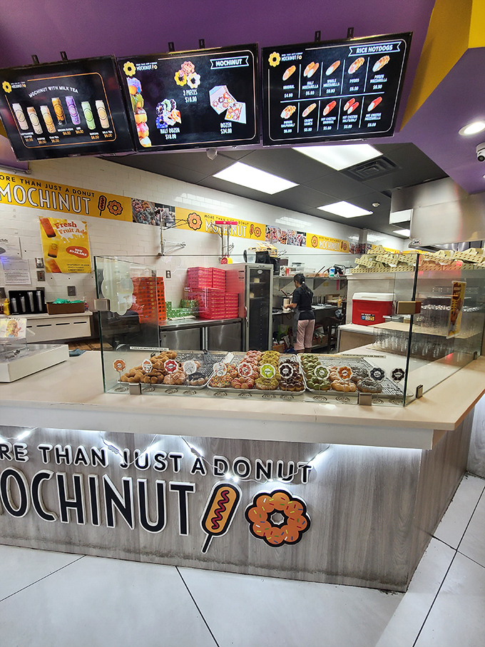 Behind the counter, a rainbow of mochi donuts awaits, each tray a different flavor expedition ready for the taking.