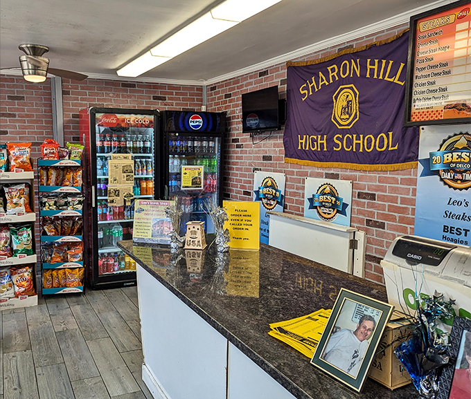 Local pride on full display with the Sharon Hill High School banner, where sandwich artistry happens beneath fluorescent lights and decades of community connection.