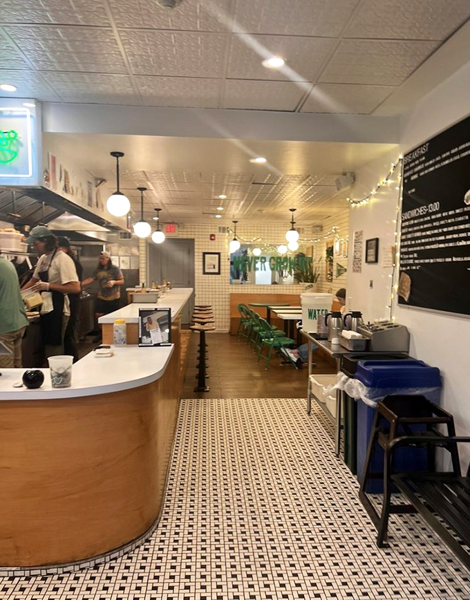 Inside, minimalist design meets deli comfort with white tile floors, wooden accents, and pendant lighting creating the perfect backdrop for sandwich artistry.