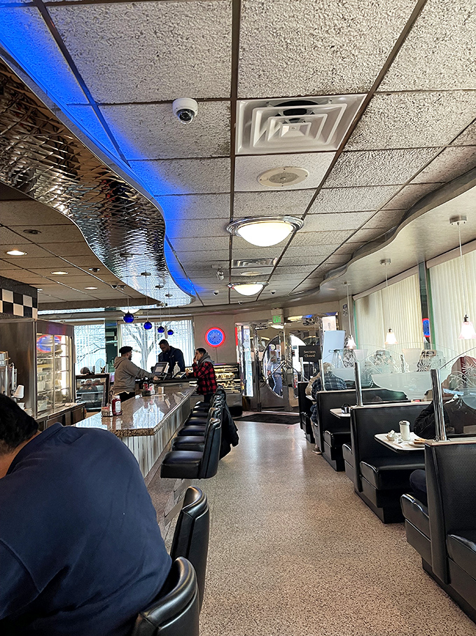 Classic diner magic happens under blue accent lighting, where counter seats offer front-row views to short-order wizardry and the symphony of sizzling griddles.