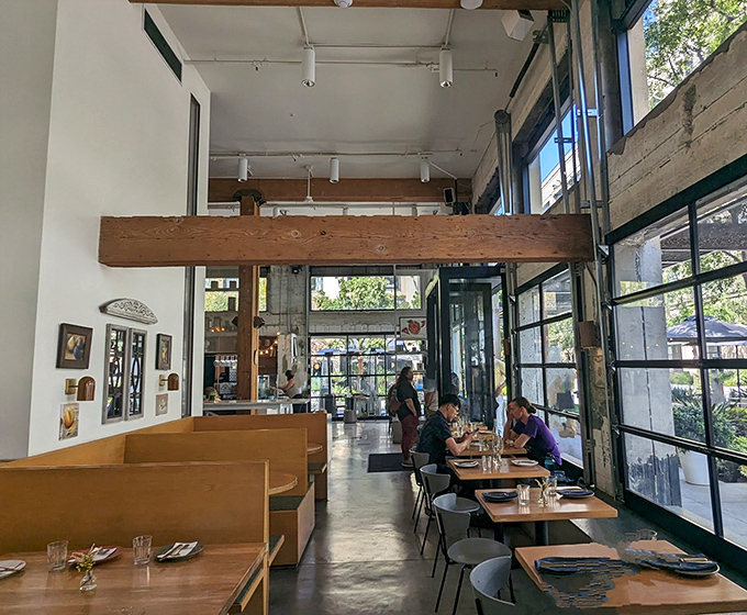 Inside, sunlight streams through floor-to-ceiling windows, illuminating wooden beams and minimalist furnishings&mdash;proof that great pizza needs no elaborate backdrop.