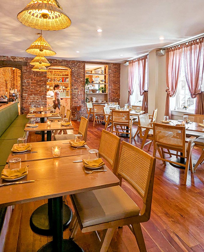 Warm wooden floors and exposed brick walls create a cozy atmosphere, while wicker lampshades cast a honeyed glow over diners.