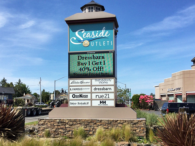 Seaside's lighthouse-inspired outlet sign shines bright against Oregon's blue sky, a landmark for coastal bargain hunters.
