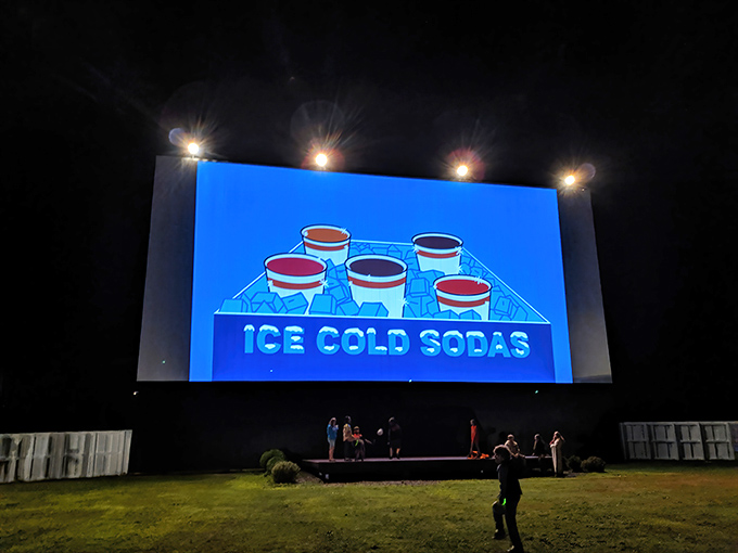 Cars gather like fireflies drawn to the giant screen, creating a constellation of tail lights against the evening sky.