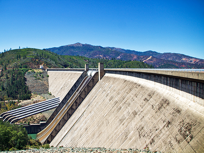 Shasta Dam stands like a concrete giant, holding back enough water to make your property values smile.