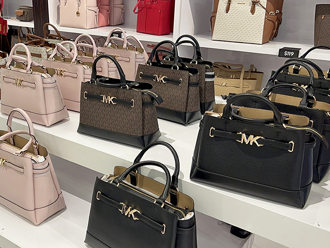 Michael Kors handbags arranged like precious artifacts, each one promising to organize your life better than Marie Kondo ever could.