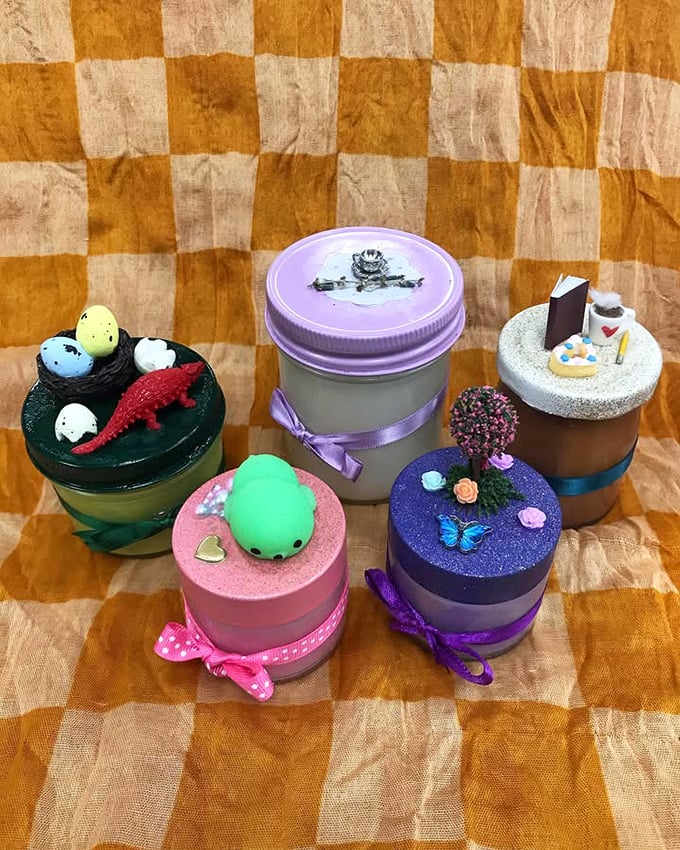 Whimsical handcrafted candles transform ordinary jars into miniature worlds of dinosaurs, sweets, and springtime gardens—affordable art for everyday life.