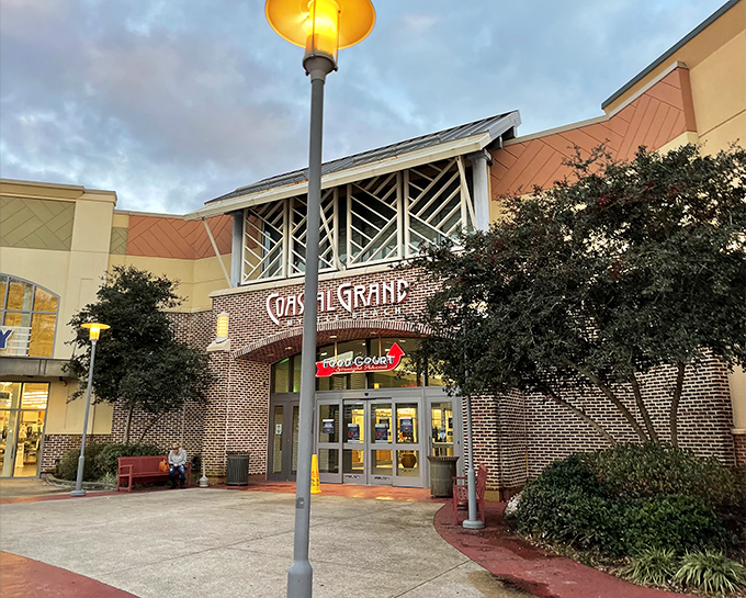 As evening approaches, Coastal Grand's brick facade and illuminated entrance transform from shopping center to community landmark.