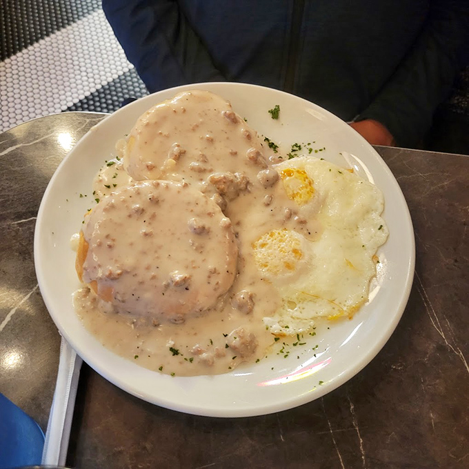 Behold the holy grail of Southern comfort: biscuits drowning in peppery sausage gravy alongside sunny-side-up eggs that wink at you from the plate.