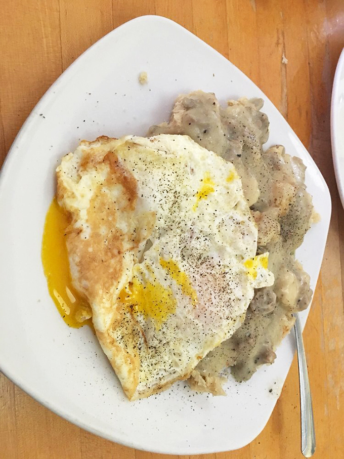 Behold the holy grail of comfort food: cloud-like biscuits swimming in peppery gravy, topped with eggs that surrender their golden yolks on first touch.