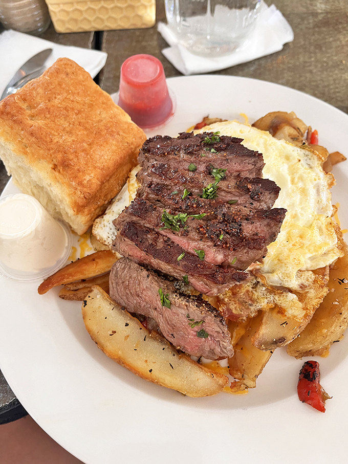 Steak and eggs reimagined as a masterpiece&mdash;where perfectly seared beef meets golden potatoes and that biscuit stands tall like a carb-loaded monument to breakfast excellence.
