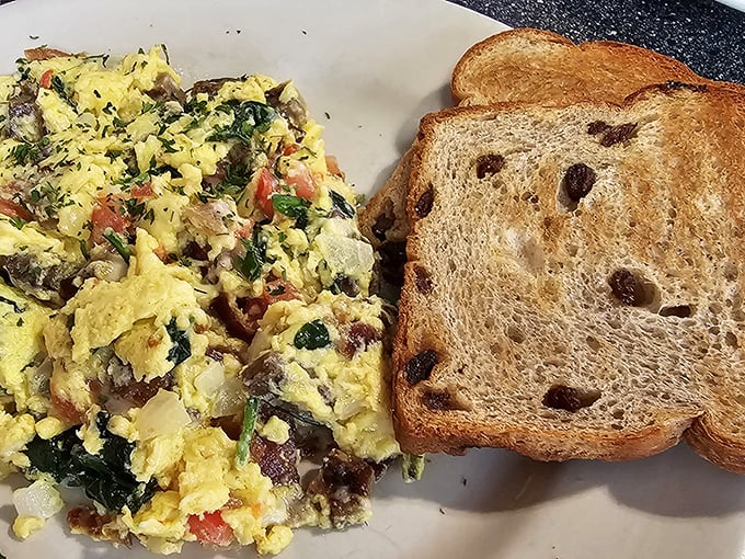 Scrambled eggs loaded with veggies alongside cinnamon raisin toast – proof that "eating your vegetables" can actually be the highlight of breakfast.