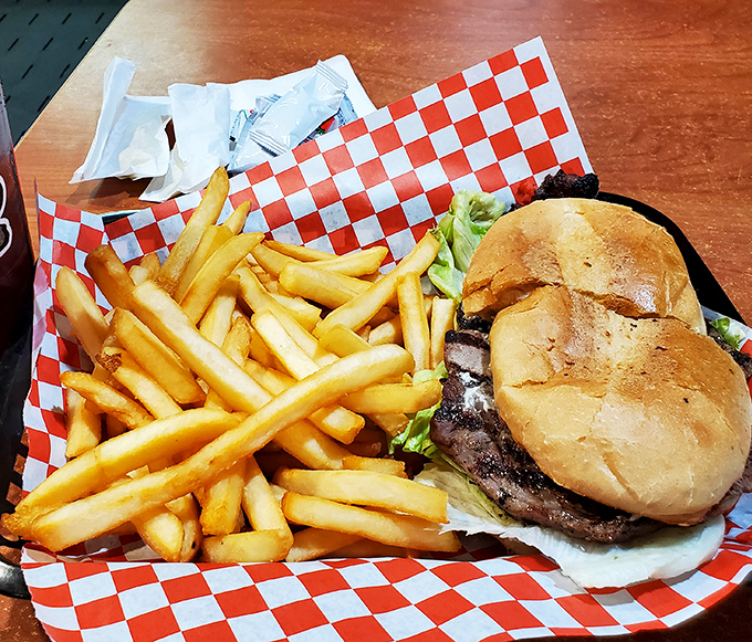 Behold: the burger in its natural habitat. Golden fries standing at attention beside their beefy commander. A red-checkered battlefield where no morsel survives.