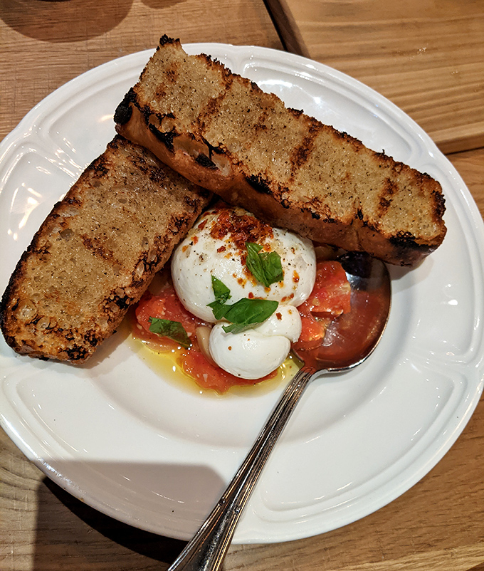 The legendary burrata arrives like a cloud of dairy perfection, surrounded by tomatoes that clearly lived their best life.