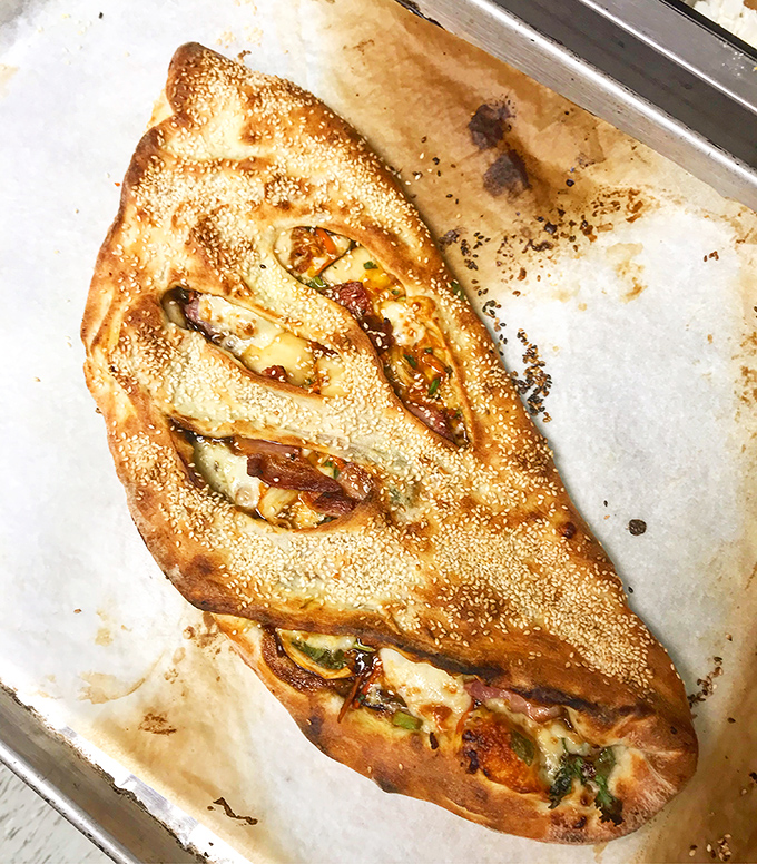 Golden-brown perfection with a hint of what's inside peeking through those artistic slashes &ndash; this calzone isn't just food, it's edible architecture.