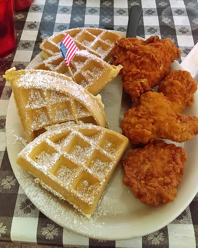 Behold the star attraction: golden-brown chicken with perfectly powdered Belgian waffles. That tiny American flag isn't just patriotic—it's marking territory in the breakfast hall of fame.