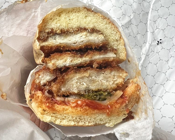 The chicken cutlet sandwich in cross-section reveals its secrets&mdash;crispy exterior, juicy interior, and that vibrant sauce creating sandwich perfection.