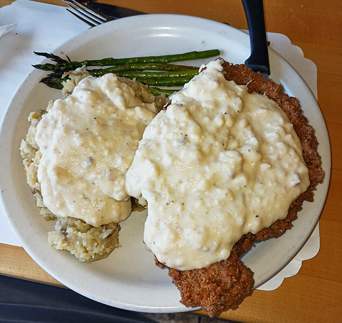 Behold the star attraction: chicken fried steak smothered in creamy gravy with a side of asparagus. This isn't just breakfast&mdash;it's edible therapy.